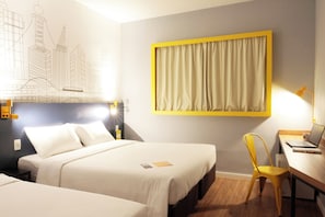 Quarto de hotel com duas camas, uma secretária com um laptop, uma cadeira e uma cortina.
