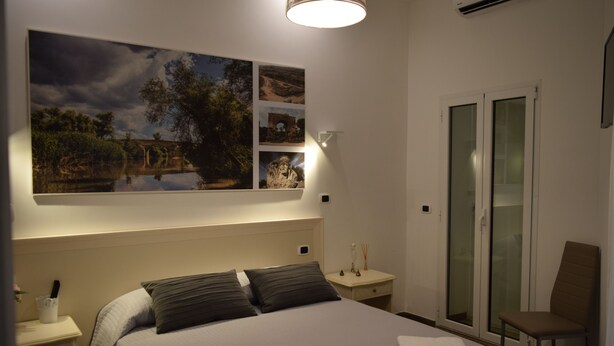 Um quarto com uma cama grande, uma mesa de cabeceira, uma cadeira, uma luminária na parede e uma porta de vidro deslizante.