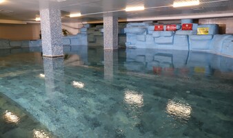 Piscina interior com água cristalina, paredes azulejadas e placas de segurança.