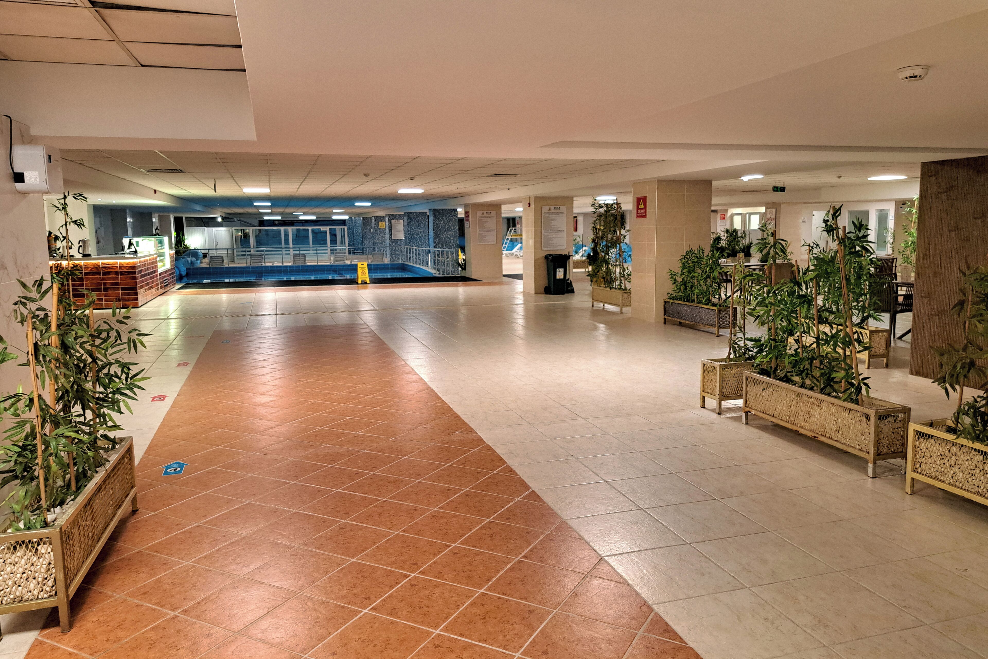 Um hall amplo com uma mesa de recepção, área de piscina azul e plantas em vasos.