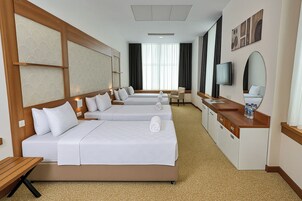 Quarto de hotel com duas camas, uma escrivaninha, televisão e uma janela grande com cortinas.
