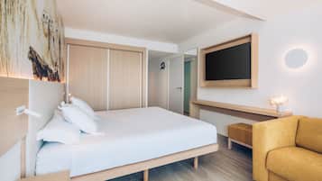 Quarto de hotel moderno com uma cama grande, uma escrivaninha, um sofá e uma televisão na parede.
