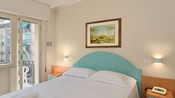 Quarto com cama, mesa de cabeceira, um quadro na parede e janela com vista para edifícios.