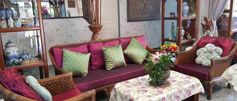 Uma sala de estar acolhedora com um sofá, duas poltronas de vime, um armário de madeira e uma mesa com toalha florida.