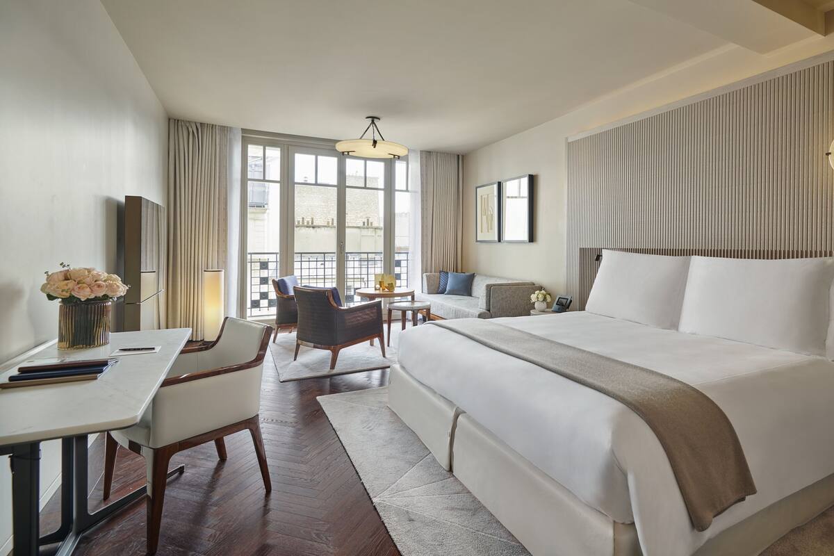 Quarto de hotel com uma cama grande, uma escrivaninha, uma cadeira, um sofá e uma varanda com vista.