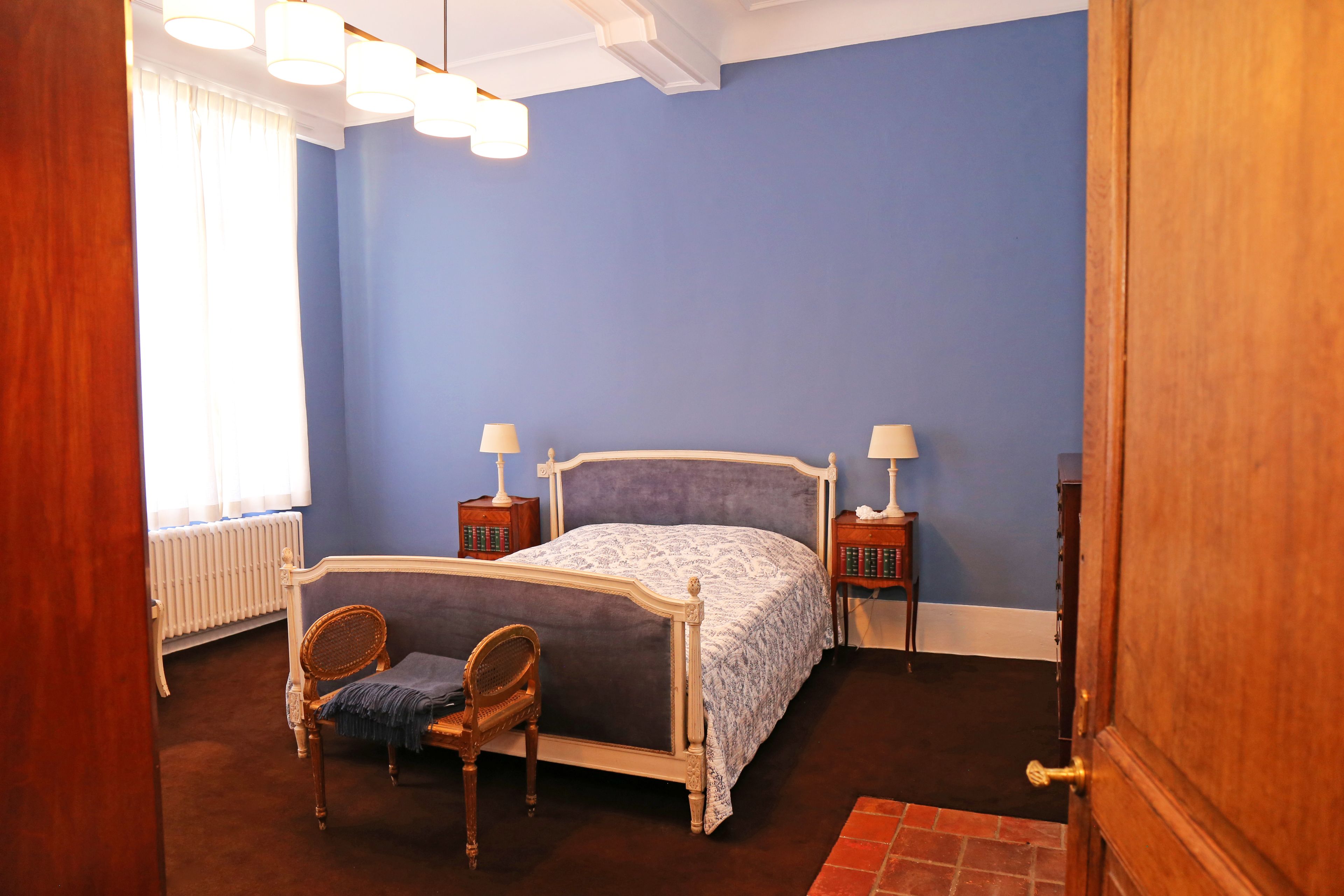 Quarto com cama, duas mesas de cabeceira, uma cadeira e um radiador.