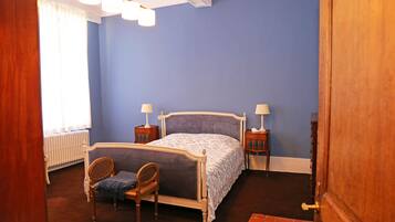 Quarto com cama, duas mesas de cabeceira, uma cadeira e um radiador.