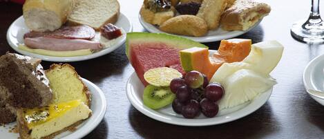 Três pratos de comida com pães, presunto, queijo e frutas diversas.