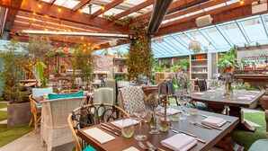 Restaurante com jardim interno, mesas de madeira, cadeiras de vime e diversos tipos de plantas.