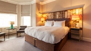Quarto de hotel com cama grande, duas mesas de cabeceira com abajures, uma cadeira e vista para o exterior.