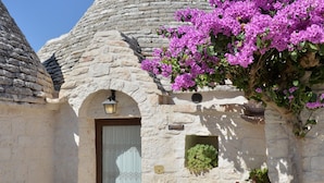 Um edifício de pedra com telhado cónico, porta de madeira e mesa com cadeiras à porta.
