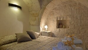 Quarto com parede de pedra, cama com roupa de cama estampada, mesa de cabeceira com abajur e toalhas sobre a cama.