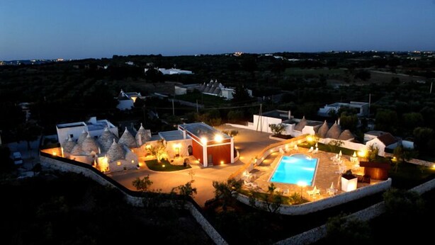 Resort com vários edifícios, piscina e área externa bem iluminada ao entardecer.