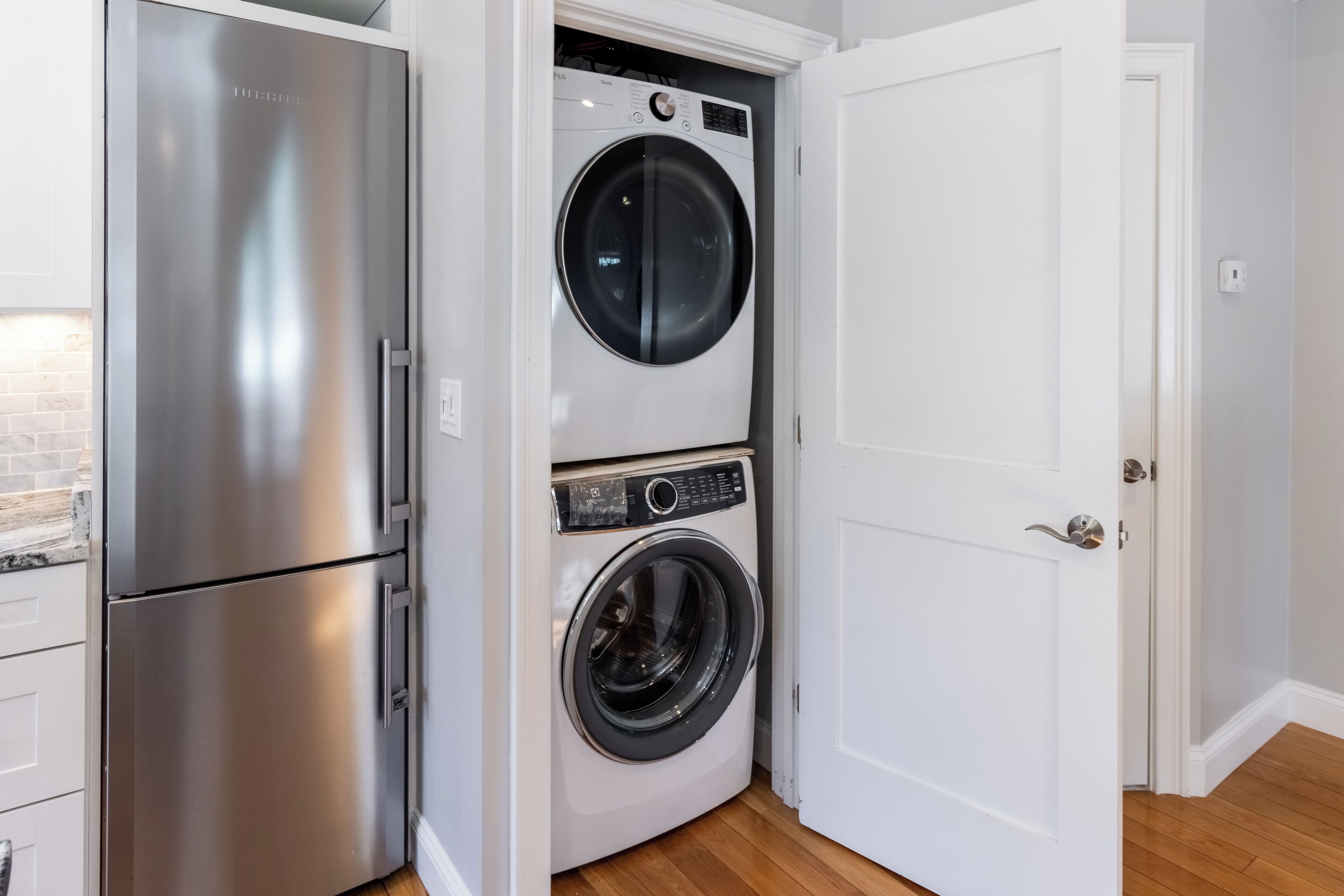 Uma lavanderia compacta com frigorífico em aço inoxidável e máquina de lavar e secar frontal.