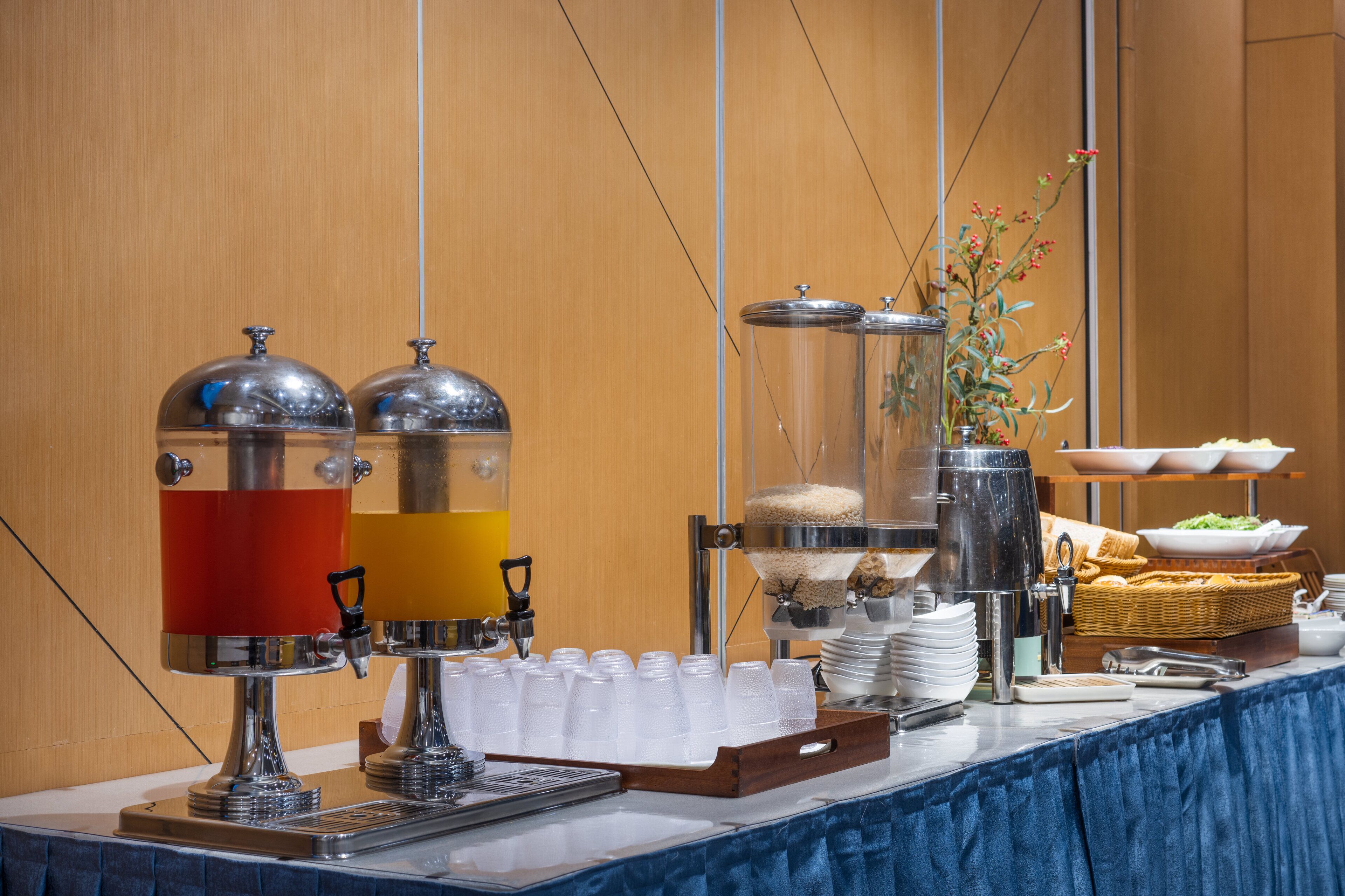 Disposição de buffet com dispensadores de bebidas, uma máquina de café e diversas opções de comida.