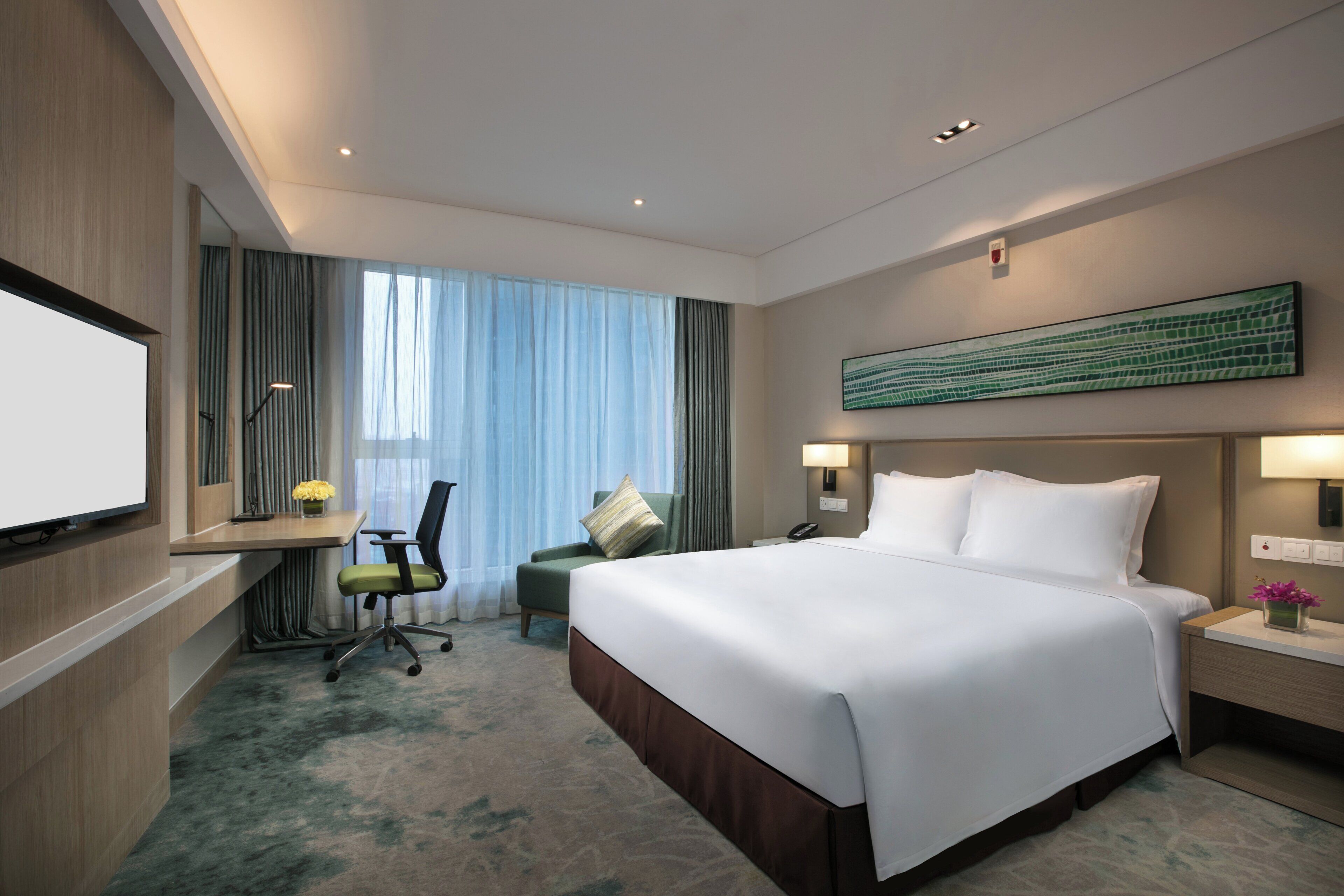 Quarto de hotel com cama, escrivaninha, cadeira e uma grande janela com cortinas.