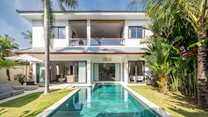 Uma casa moderna de dois andares, com piscina, área de estar externa e vegetação exuberante.