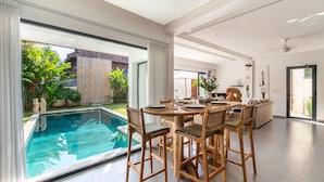Uma área de refeições moderna com vista para a piscina, mobiliário de madeira e uma grande porta de vidro deslizante.
