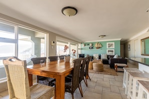 Ampla sala de estar com mesa de jantar de madeira, cadeiras de vime, um sofá e vista para o exterior.