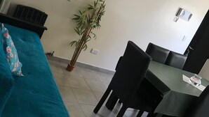 Um quarto com cama, uma mesa de jantar com cadeiras, um vaso de planta e uma janela com cortinas.
