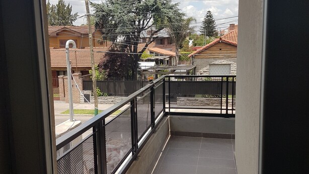 Uma varanda com grade de metal, vista de edifícios residenciais e céu claro com nuvens.