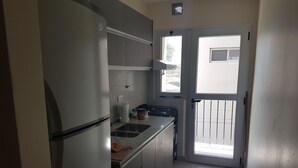 Uma cozinha compacta com geladeira, fogão e pia. É visível uma janela com vista para o exterior.