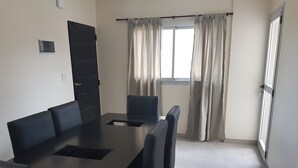 Um quarto com uma mesa de madeira escura e seis cadeiras, uma janela com cortinas e uma porta com puxador.