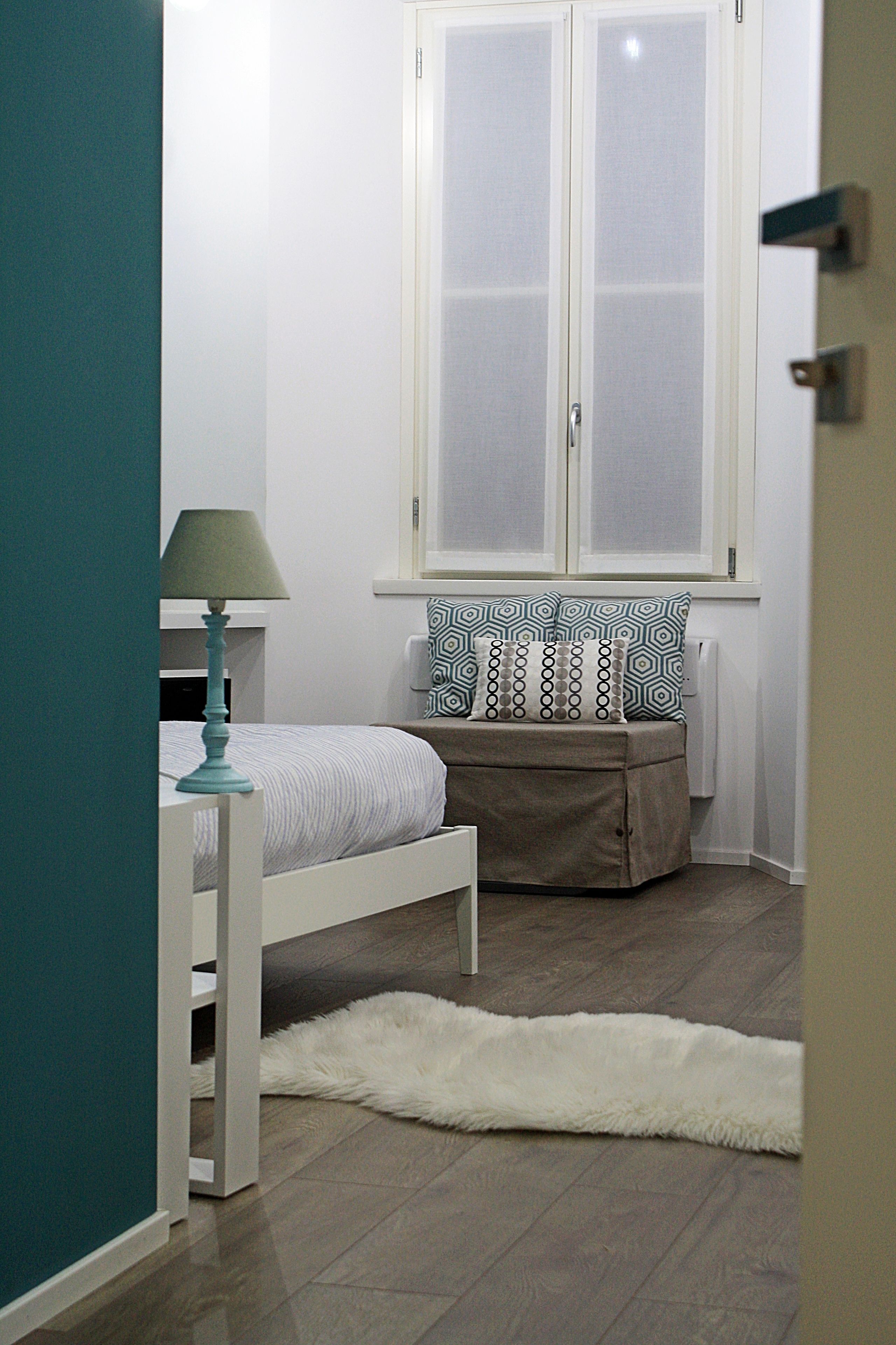 Quarto com cama, janela com persianas, luminária e tapete.