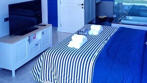 Quarto moderno com cama, televisão, guarda-roupa e banheiro visível através de uma porta de vidro.