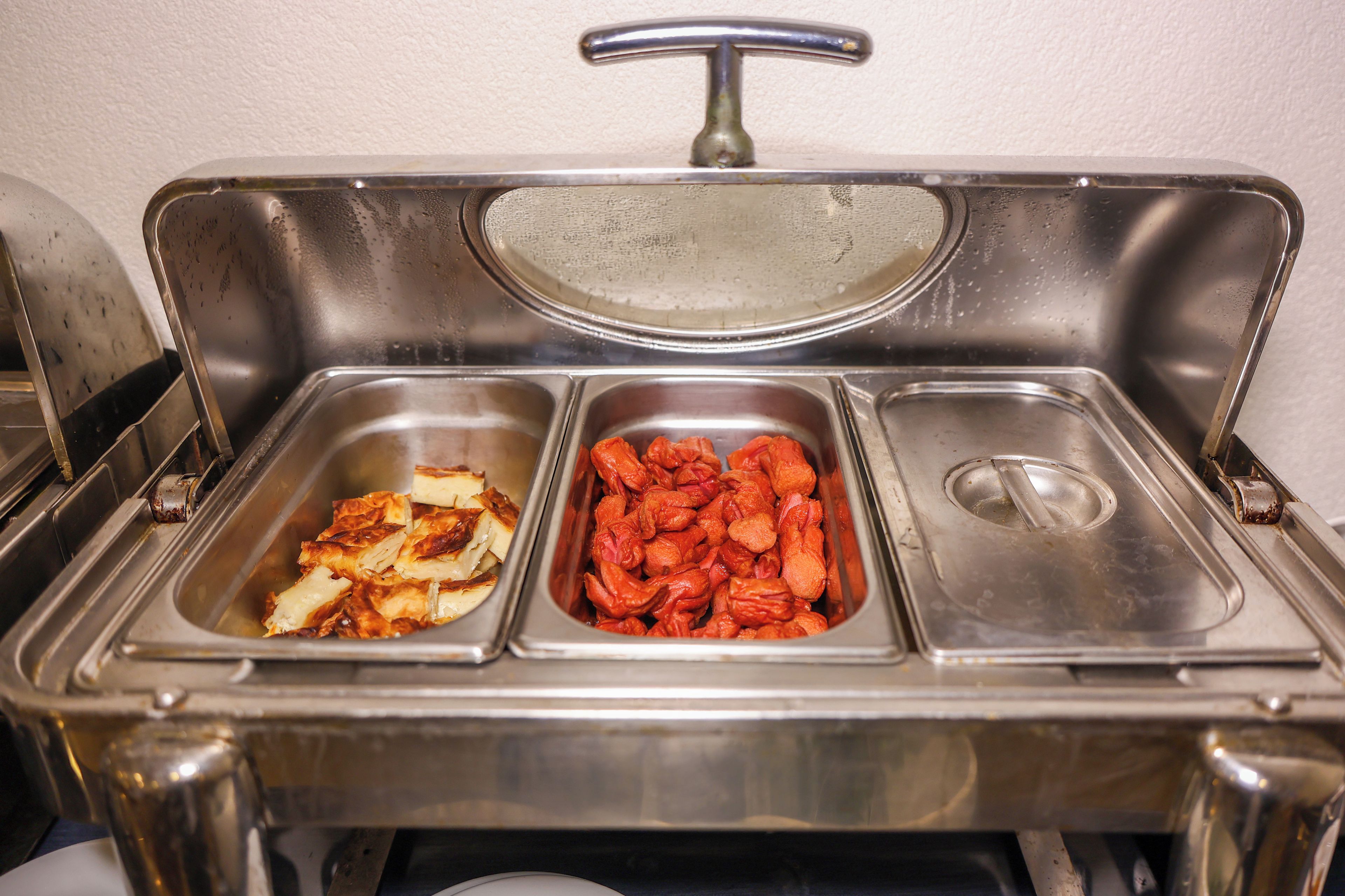 Disposição de buffet com três bandejas de metal contendo diversos alimentos.