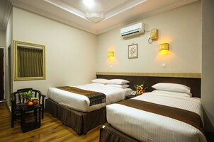 Quarto de hotel com duas camas, uma mesa com cadeira, ar condicionado e luminárias na parede.