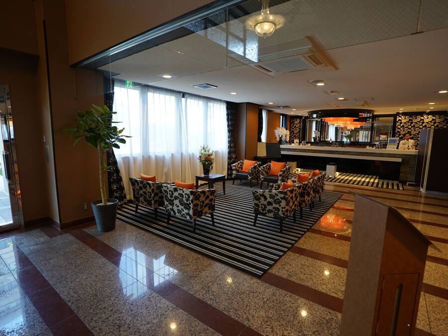 Um saguão de hotel com balcão de recepção, área de estar e uma grande planta em vaso.