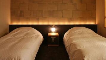 Quarto de hotel com duas camas de solteiro, uma mesa de cabeceira e parede com padrão de tijolos.