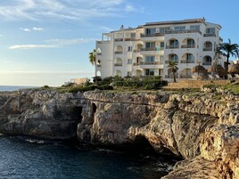 Um hotel com vários andares e varandas, situado em um penhasco com vista para o mar.
