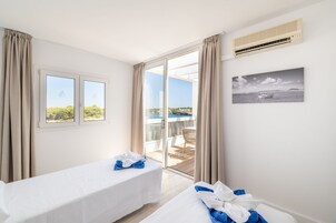 Quarto de hotel com duas camas, varanda com vista para o mar e um quadro na parede.