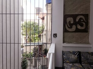 Um quarto com janela protegida por grades, parede branca com obra de arte abstrata em preto e branco, e um sofá estampado.