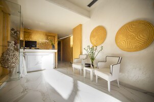 Uma área de recepção com piso de mármore, balcão de atendimento, duas cadeiras brancas e arte decorativa na parede.