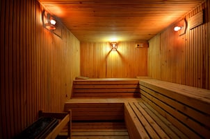 Uma sauna com bancos e paredes de madeira, e duas luminárias fixadas na parede.