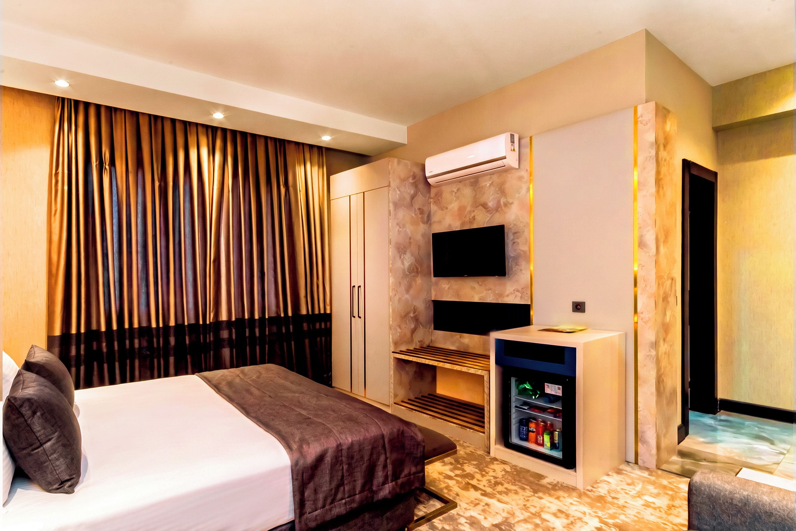 Quarto de hotel com cama, minibar, televisão e ar condicionado.