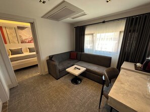 Quarto de hotel moderno com sofá, uma mesinha, uma cadeira, uma cama e uma janela com cortinas.