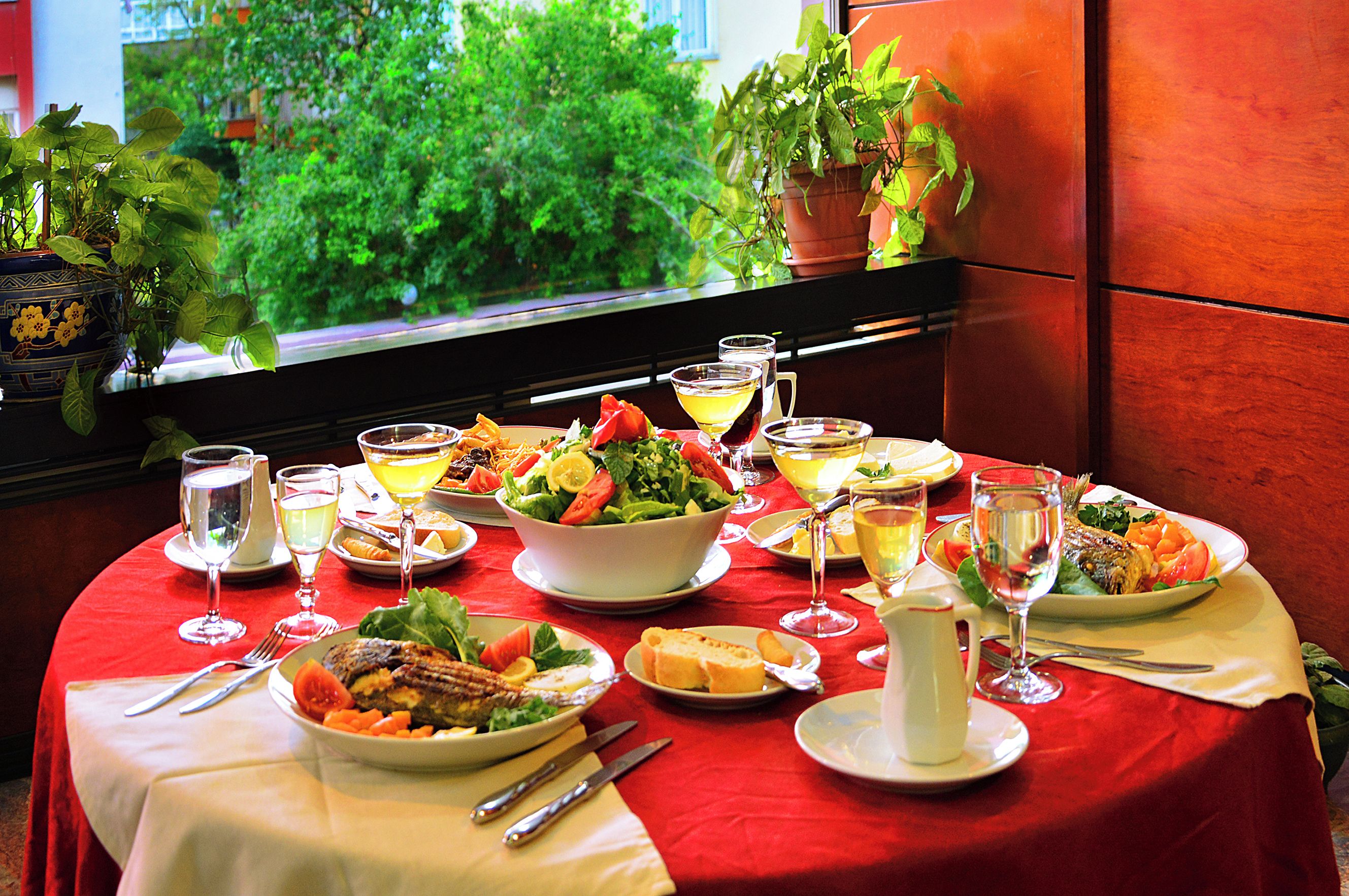 Mesa posta para refeição com diversos pratos, copos de vinho e vista para o verde lá fora.