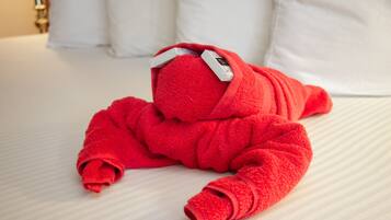Um brinquedo macio com vestimenta vermelha sobre uma cama com almofadas brancas e padrão listrado.