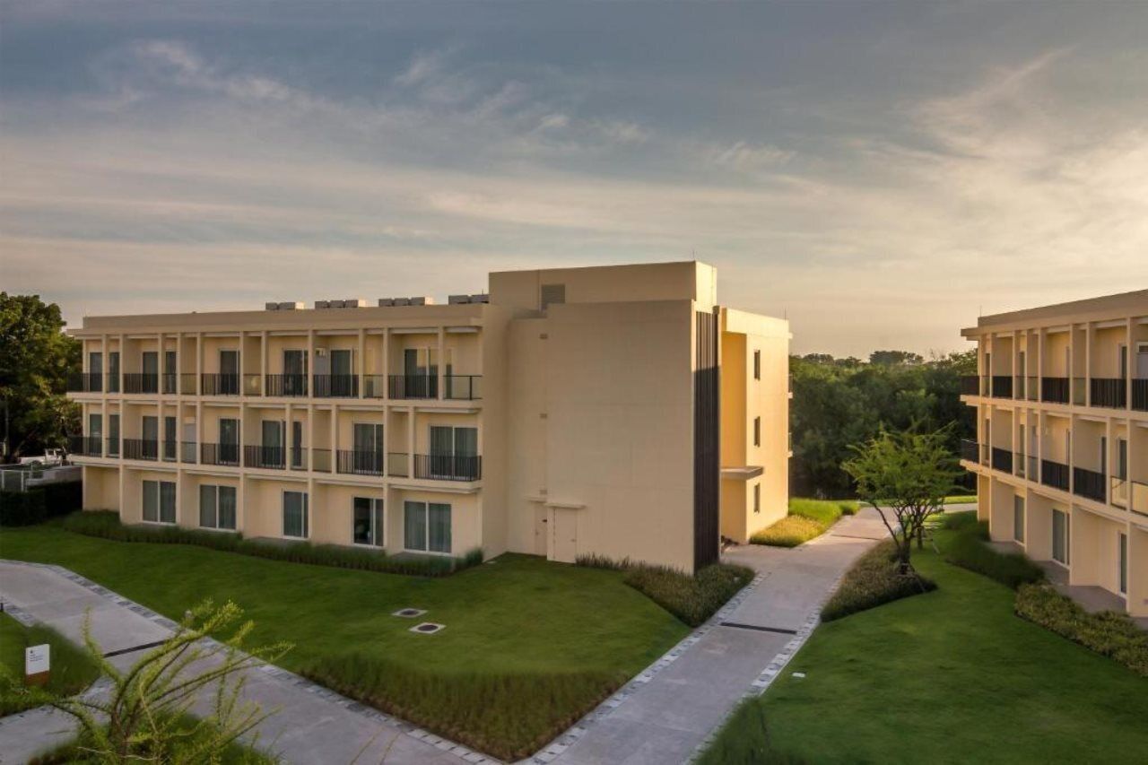Um hotel moderno de vários andares com fachada plana, várias varandas e uma área de jardim bem cuidada.