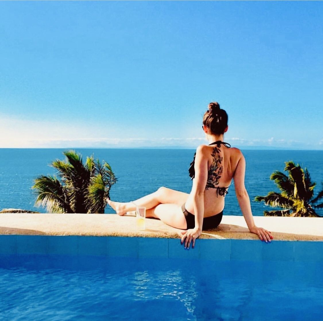 Uma pessoa sentada à beira da piscina, com vista para o oceano.