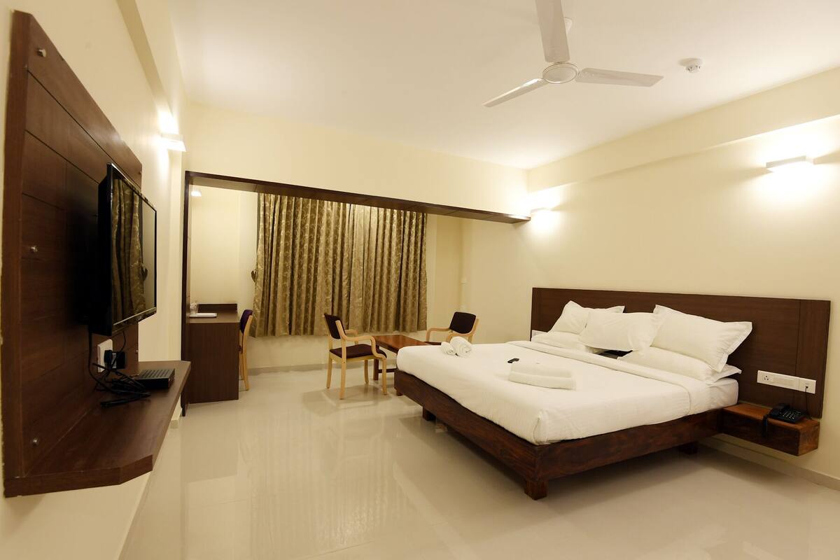 Quarto de hotel com cama, escrivaninha, cadeira, televisão e ventoinha no teto.