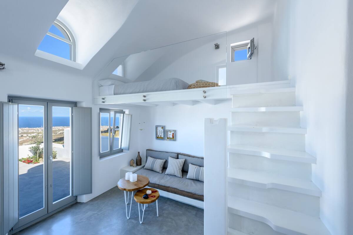 Interior moderno e claro, com um mezanino de quarto, sofá e área de jantar com vista para o mar.