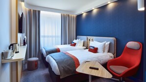 Quarto de hotel com duas camas, uma escrivaninha, uma cadeira e uma mesa pequena.
