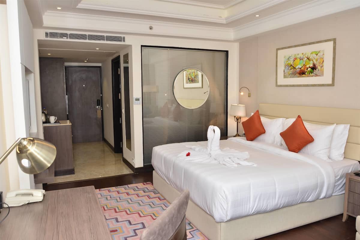 Quarto de hotel com cama, escrivaninha, cadeira, abajur, telefone, espelho e um quadro na parede.