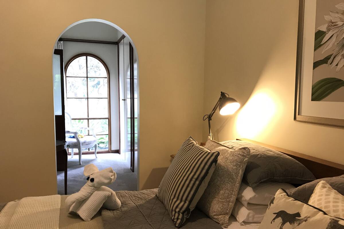 Quarto de hotel com cama, luminária, janela e porta para uma varanda.