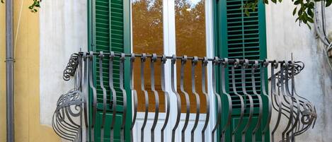 Varanda com venezianas verdes e grades de metal decoradas.